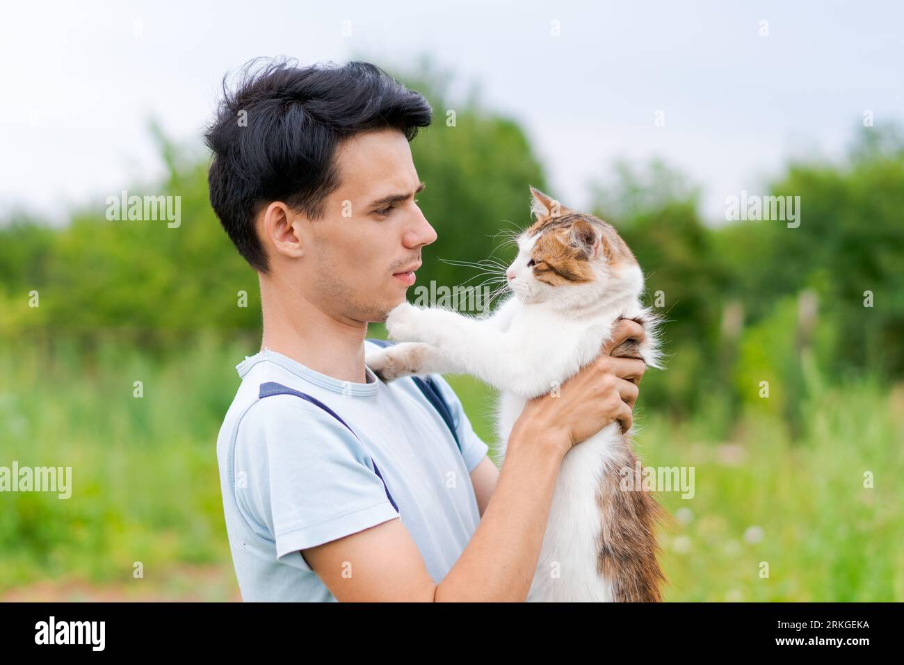 the guy holds a young cat in his arms and looks at him in the garden ...