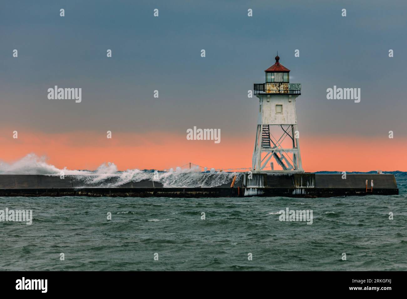 The Grand Marais Lighthouse illuminated by a vibrant sunset, with the ...