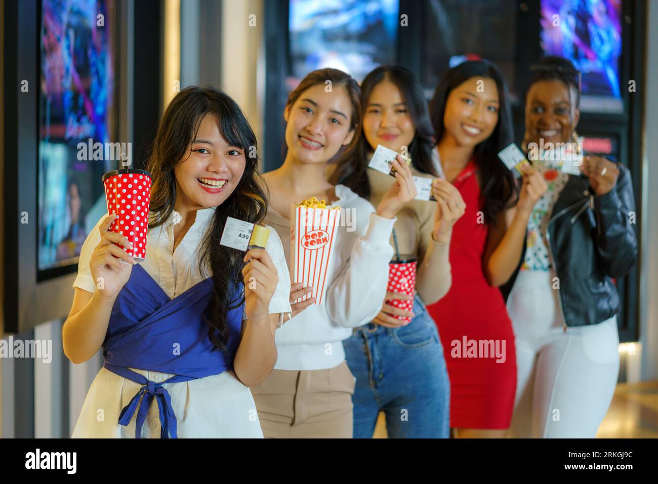 Diverse friends, popcorn in hand, stroll joyfully in front of the ...