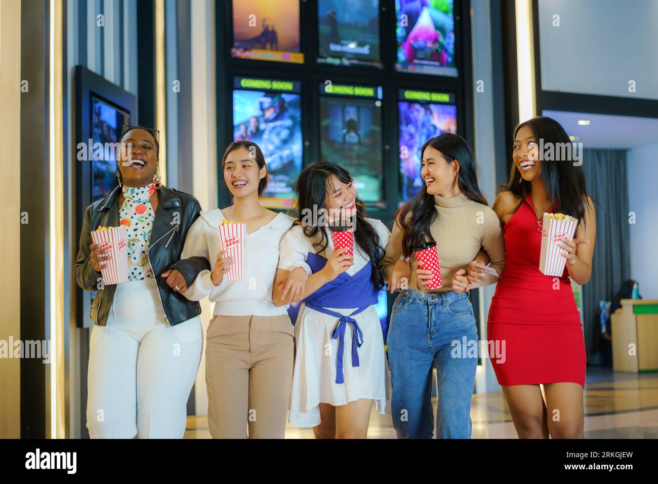 Diverse friends, popcorn in hand, stroll joyfully in front of the ...