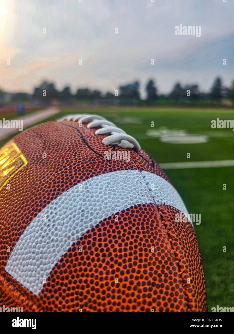 A vertical closeup of a football ball with a blur football field ...