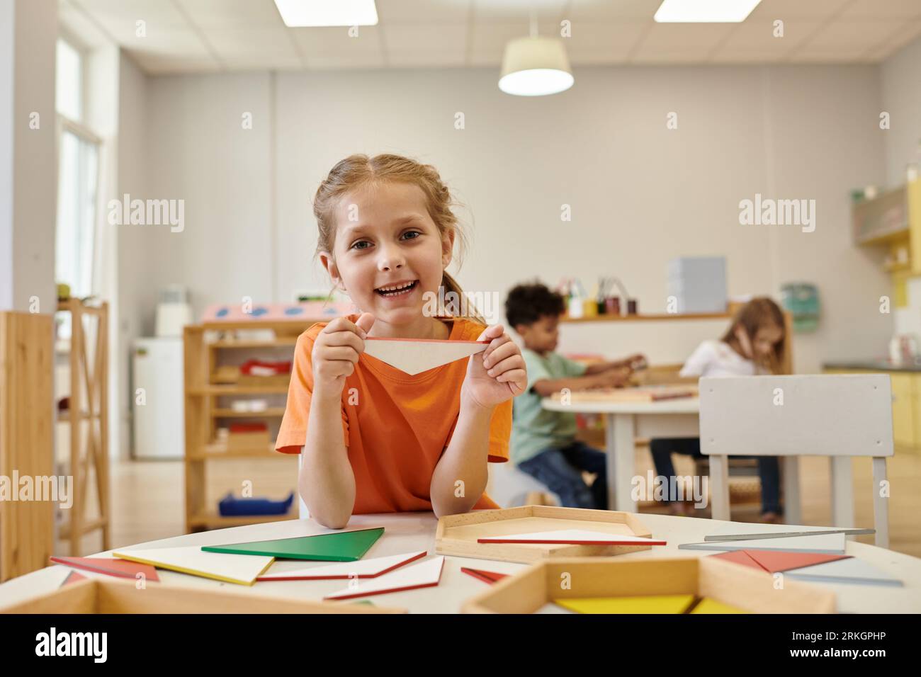positive child holding wooden triangle and looking at camera in ...