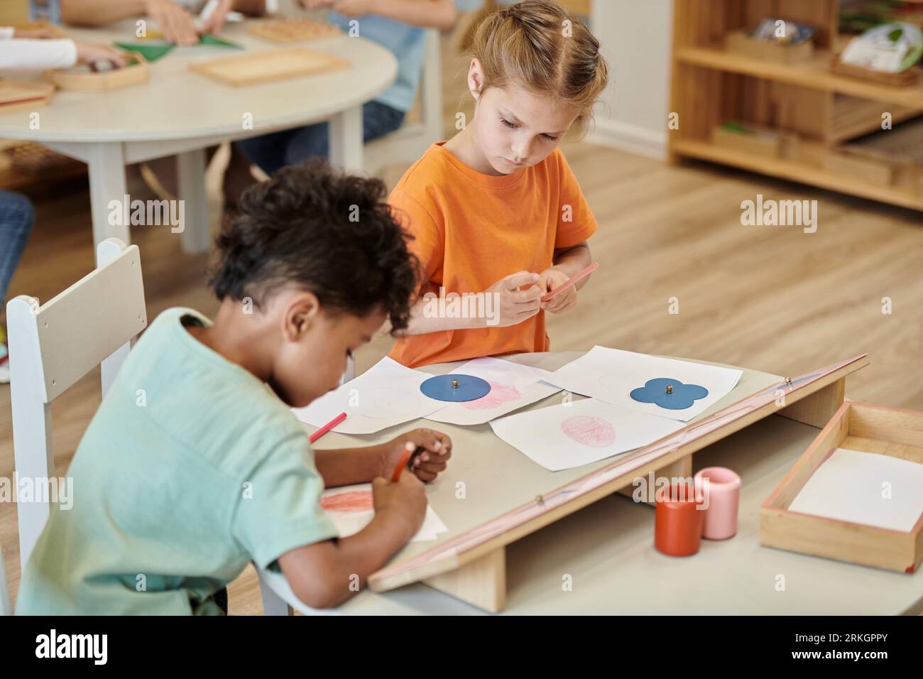 multiethnic children drawing with pencils on table in class of ...