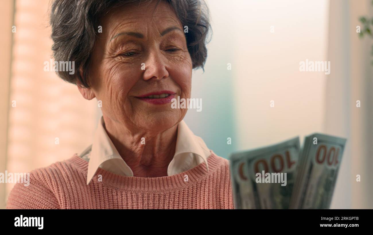 Happy smiling rich Caucasian old woman count money at home bills ...