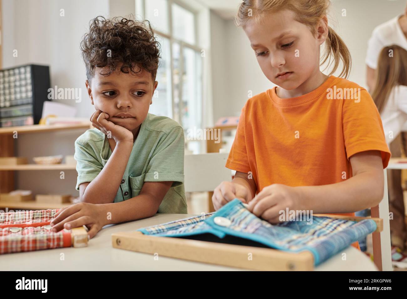 african american boy looking at friend playing with cloth and buttons ...
