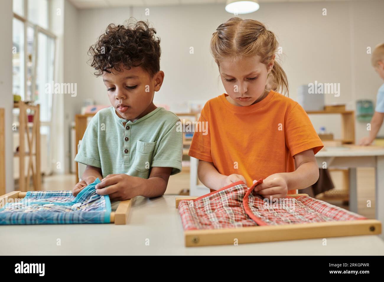multiethnic children buttoning cloth on frames in class in montessori ...