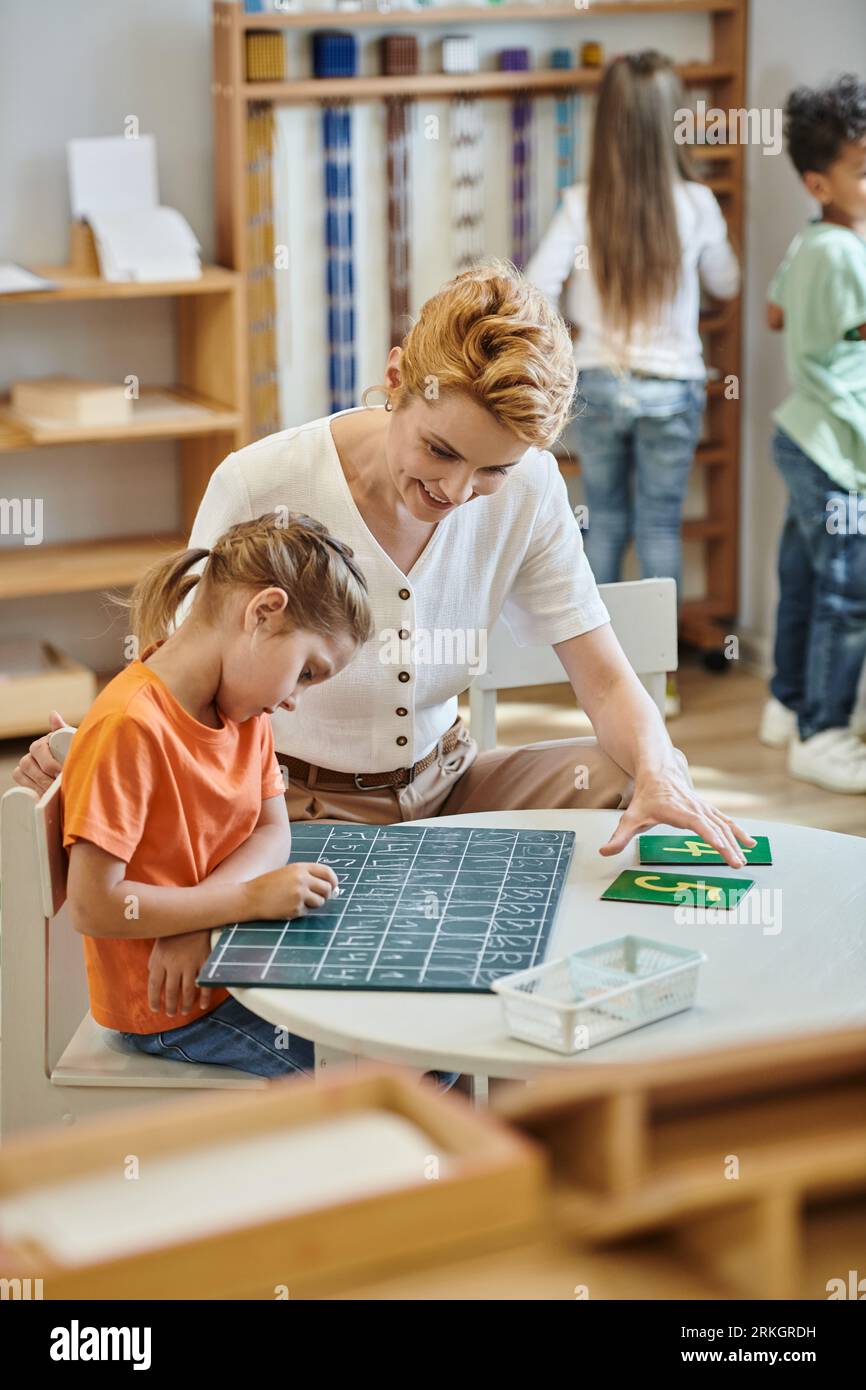 girl writing on chalkboard near numbers, learning through play, teacher ...