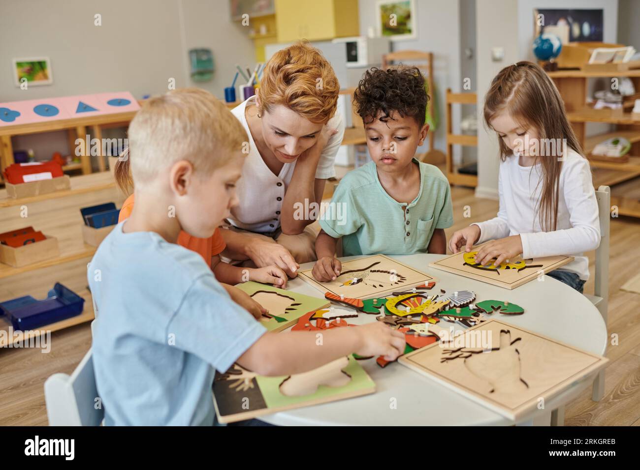 teacher talking to interracial children playing together near game on ...