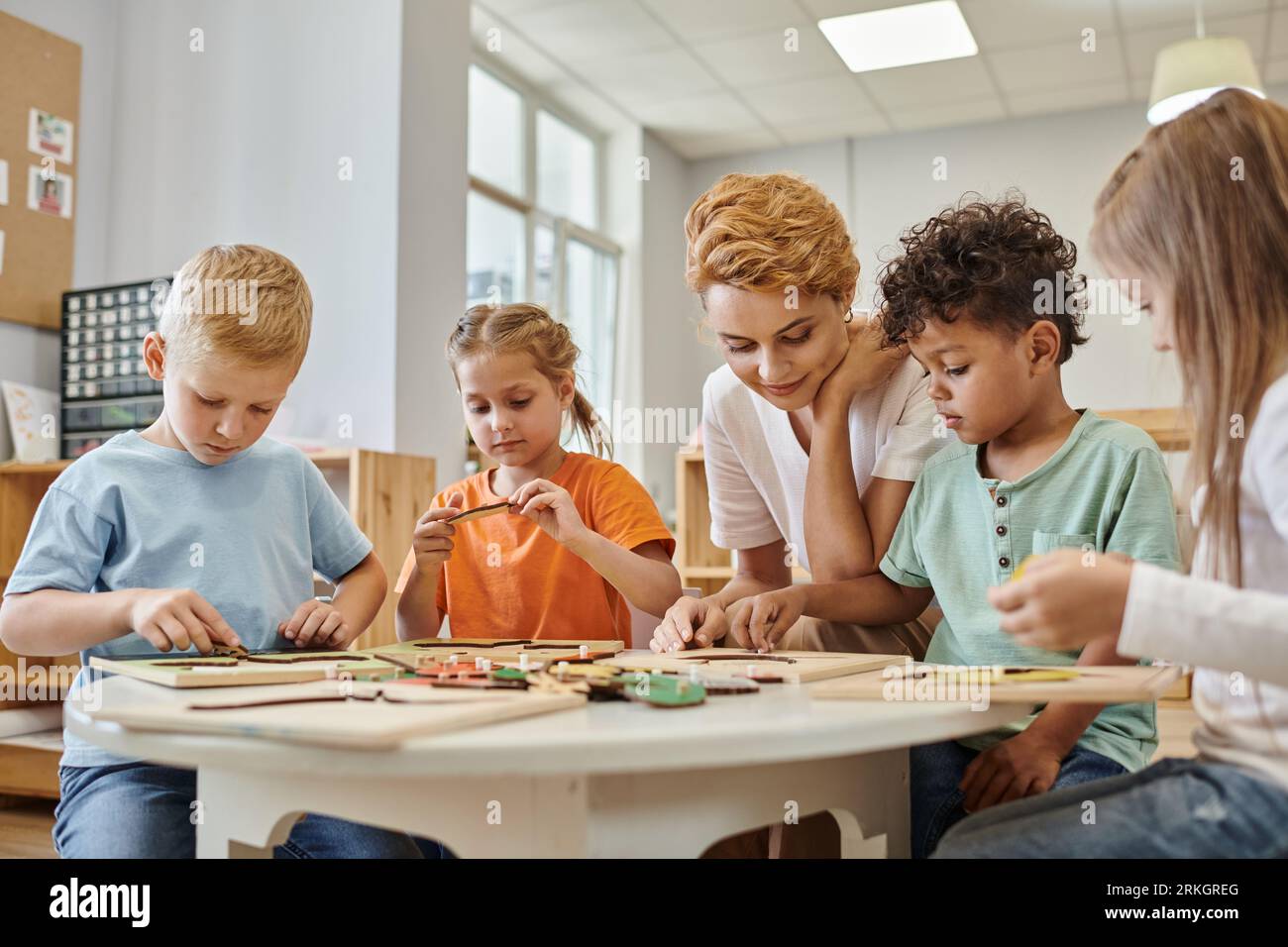 interracial children playing game near teacher in class in montessori ...