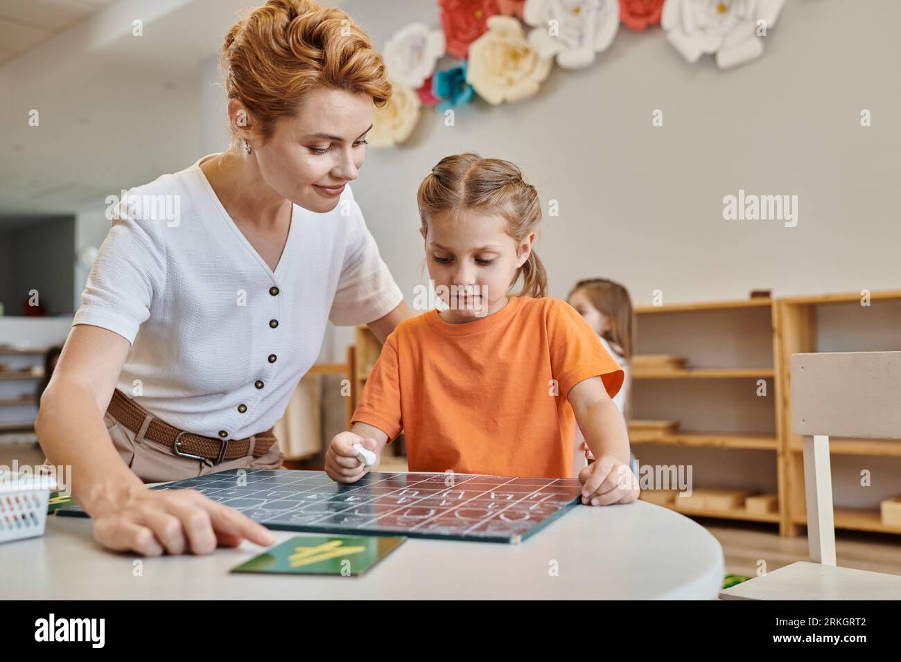 joyful teacher observing smart girl in Montessori school, counting ...