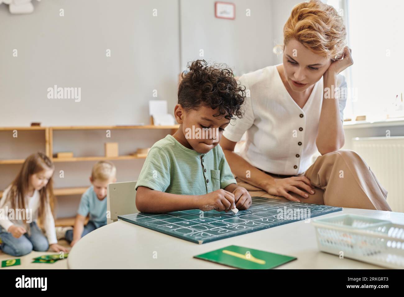 teacher talking to african american boy writing on chalkboard, counting ...