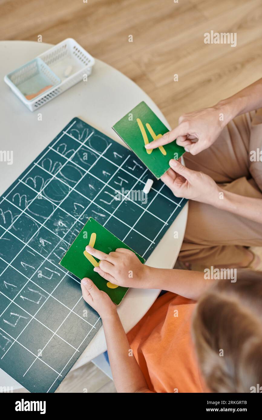 girl and teacher pointing at number near chalkboard, learning through ...