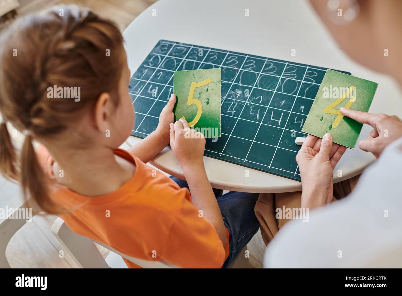 clever girl and teacher pointing at numbers near chalkboard, learning ...
