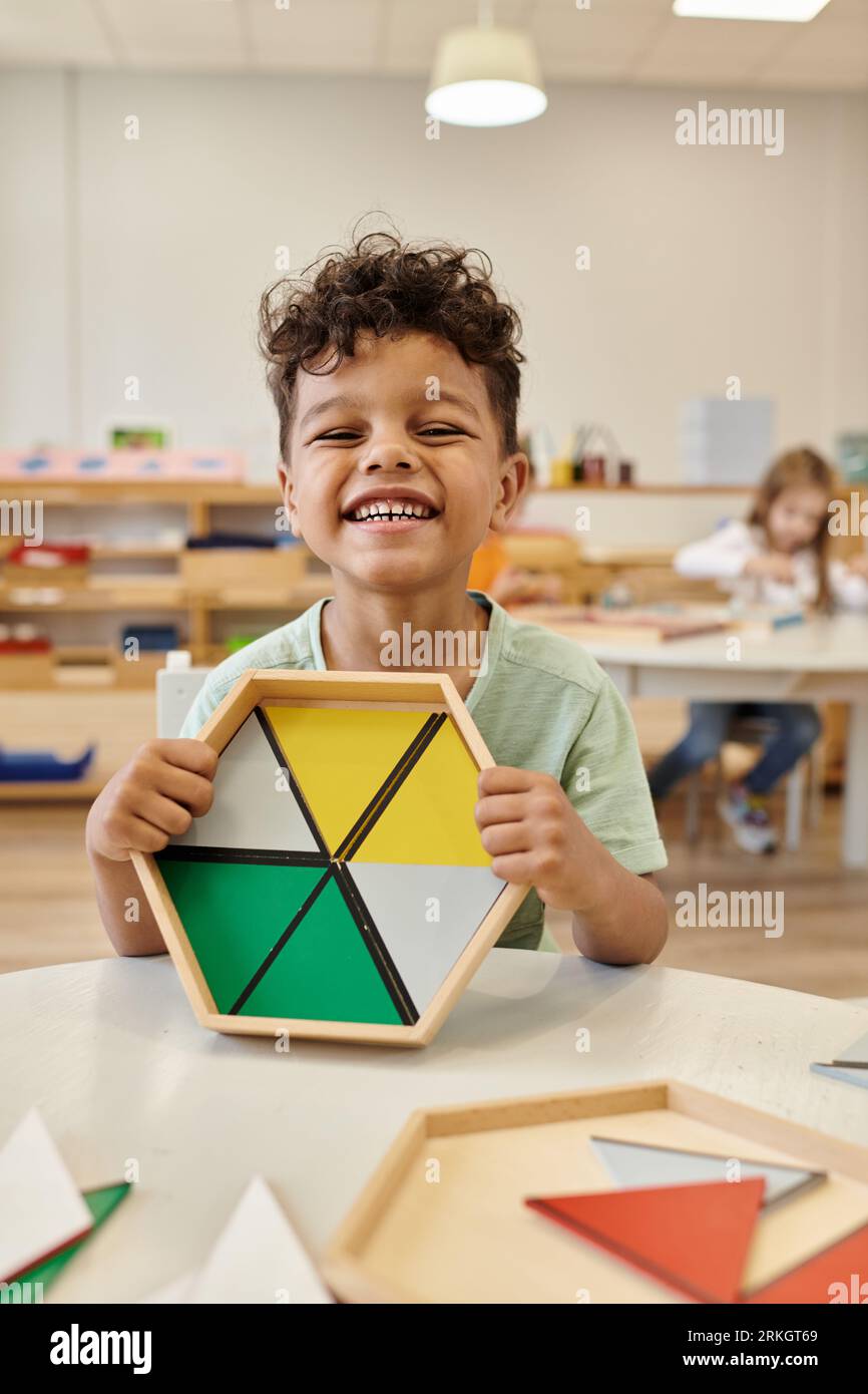 happy african american boy holding wooden game near table in class in ...