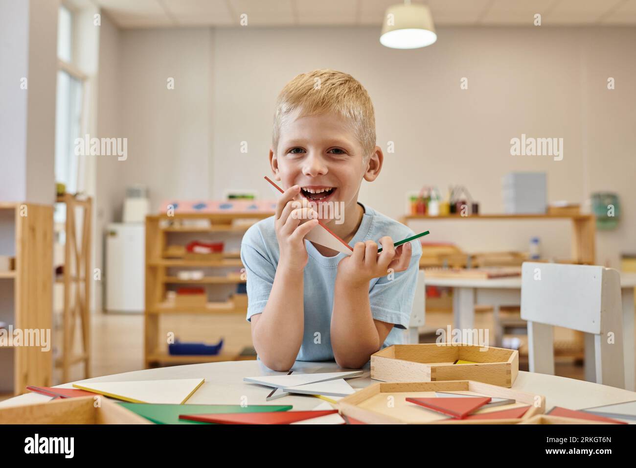 cheerful boy holding triangles during game in classroom in montessori ...