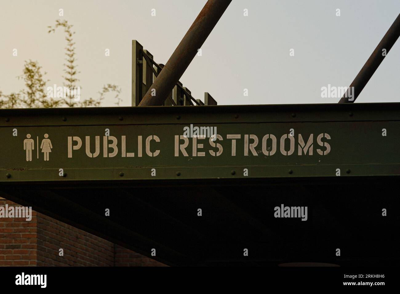 A public restrooms sign on a green metal structure in a clear sunset ...