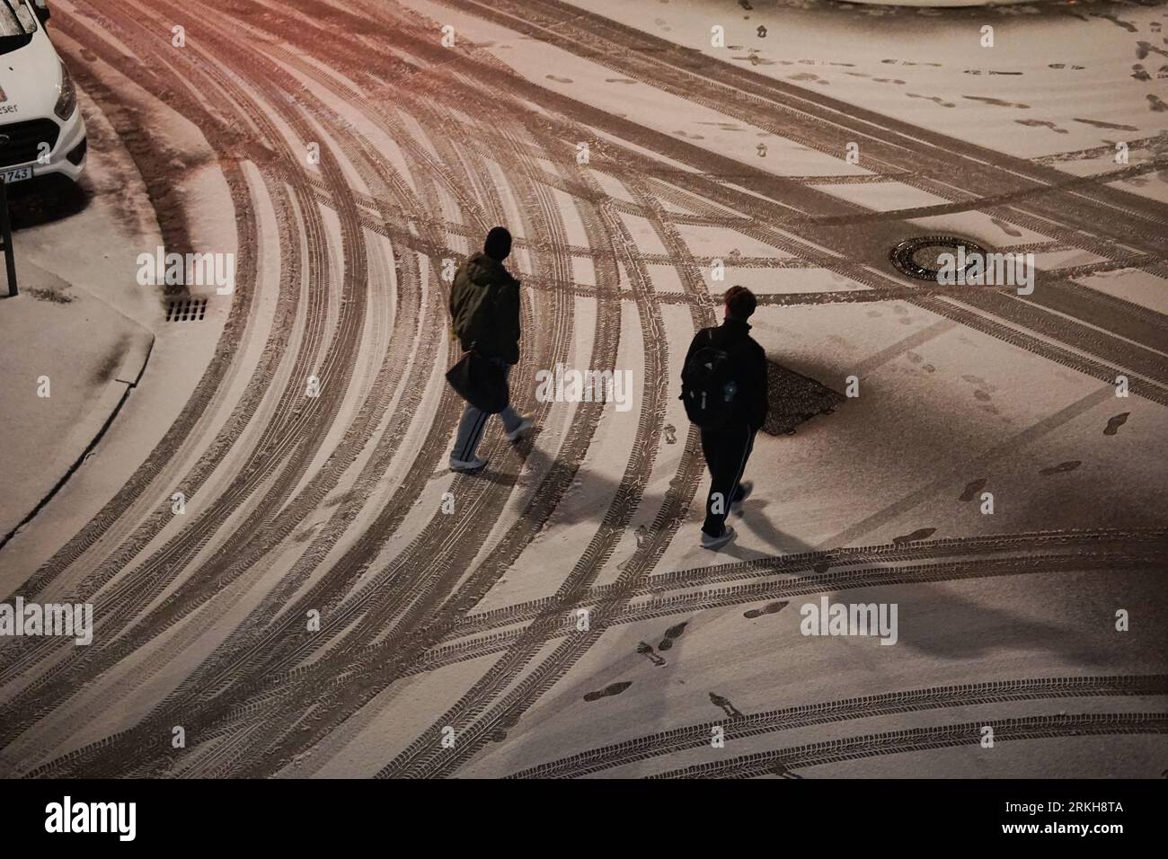 A high angle shot of two people walking on a snowy sidewalk in a winter ...
