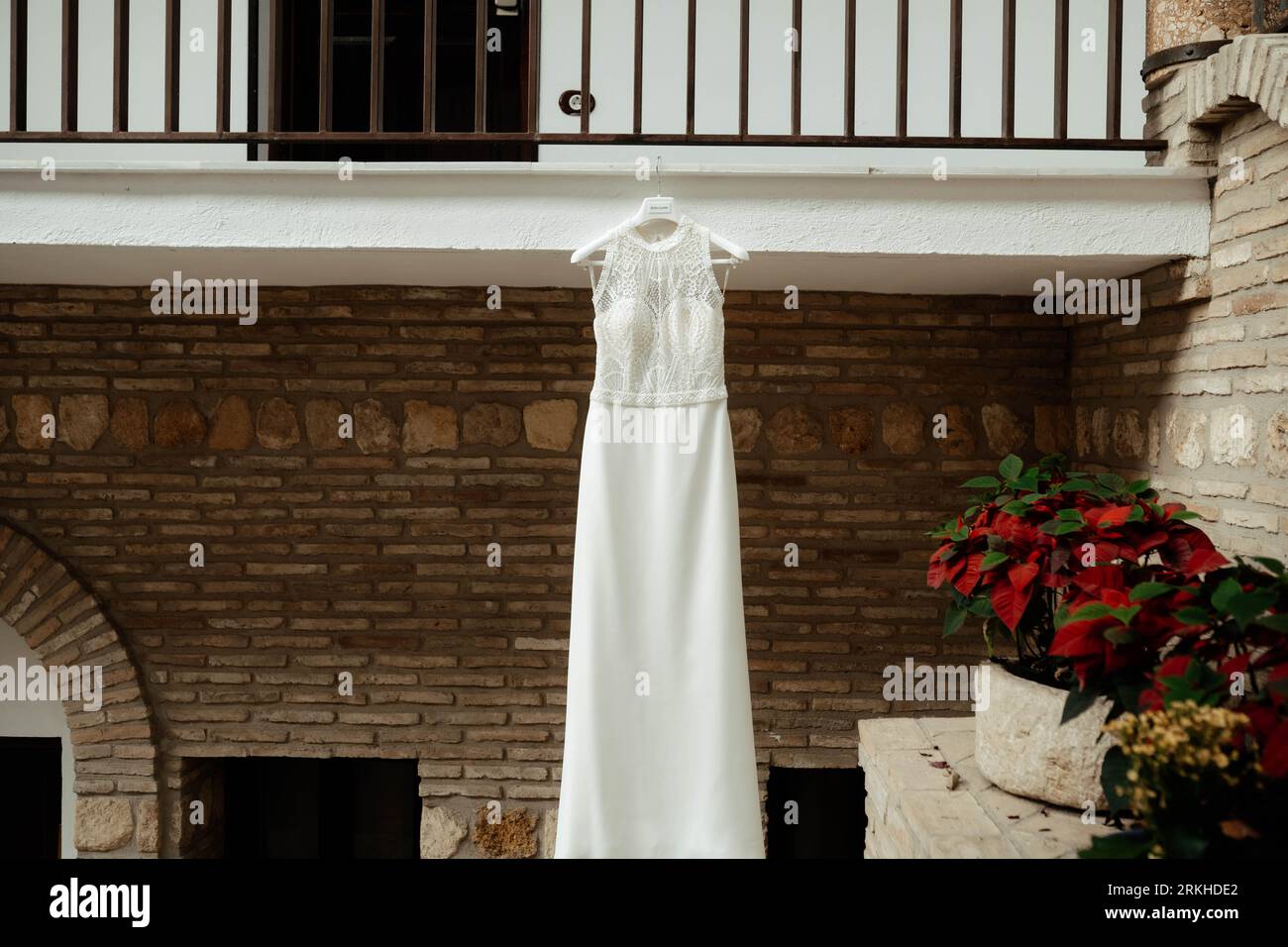 An image of a pristine white wedding dress draped over a wooden chair ...