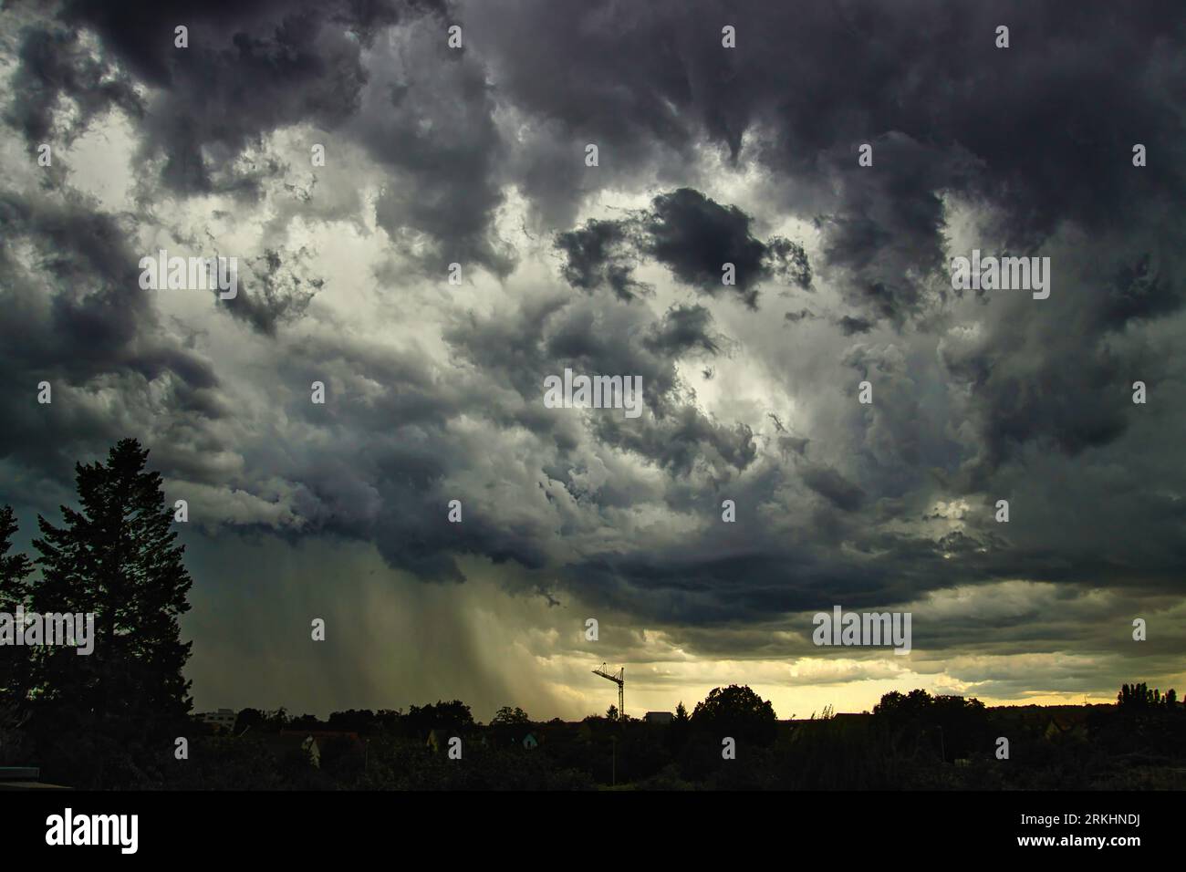 A dramatic view of a looming storm cloud in a dark sky with sun beams ...