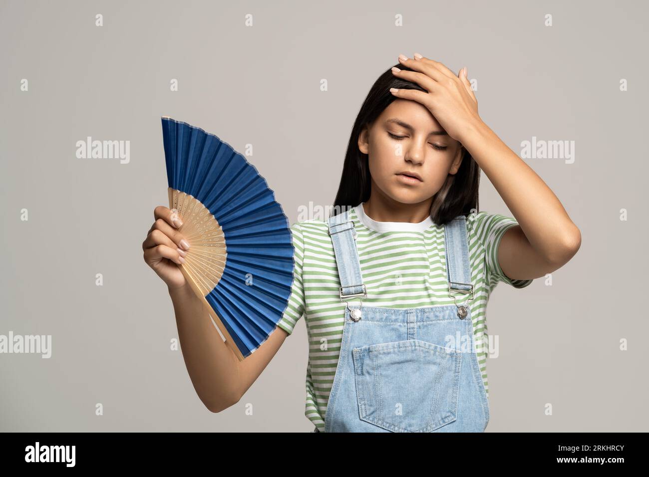 Sweaty teenage girl touching forehead using paper fan suffer from heat ...