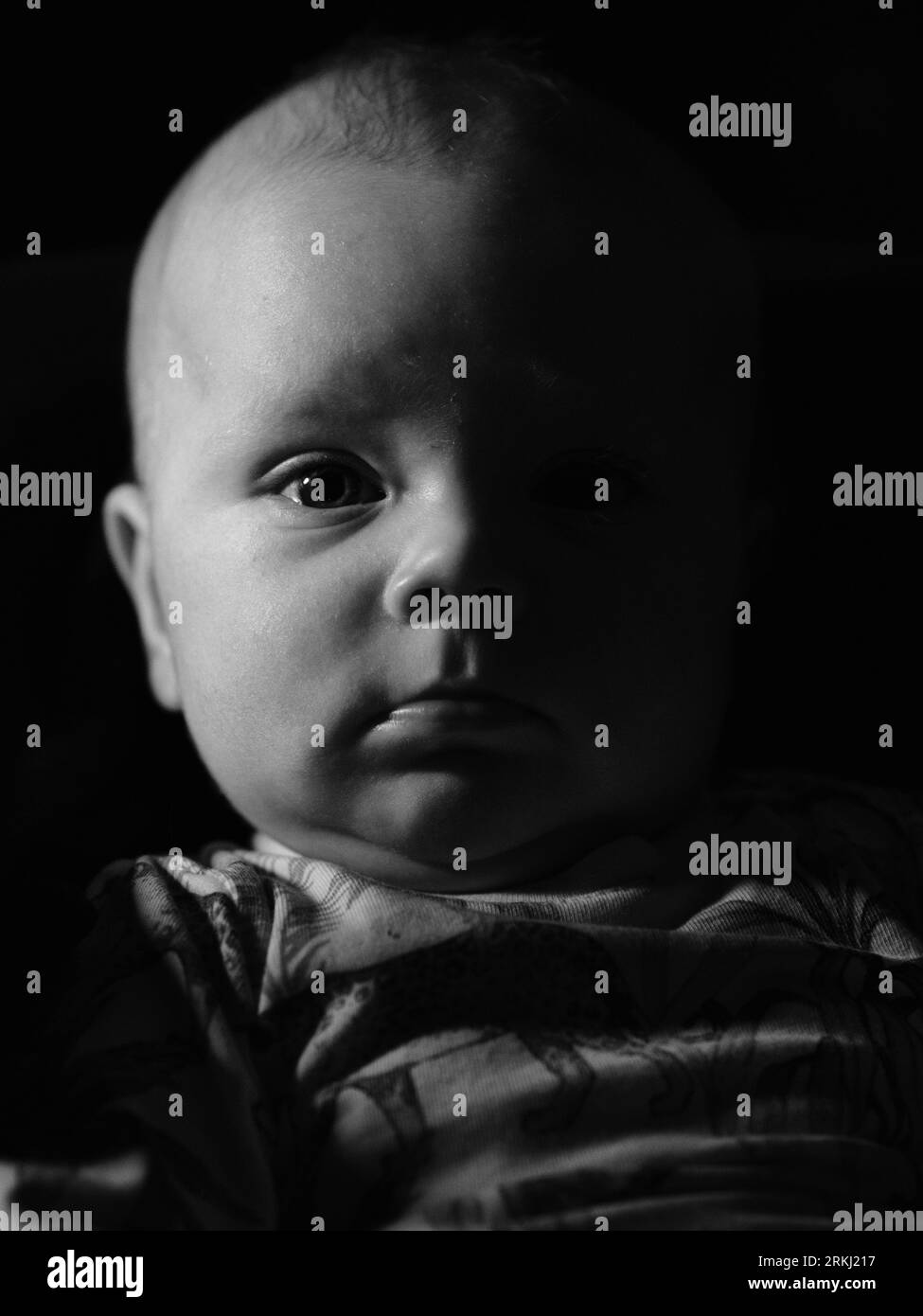 A vertical grayscale artistic shot of a cute baby in the dark Stock ...
