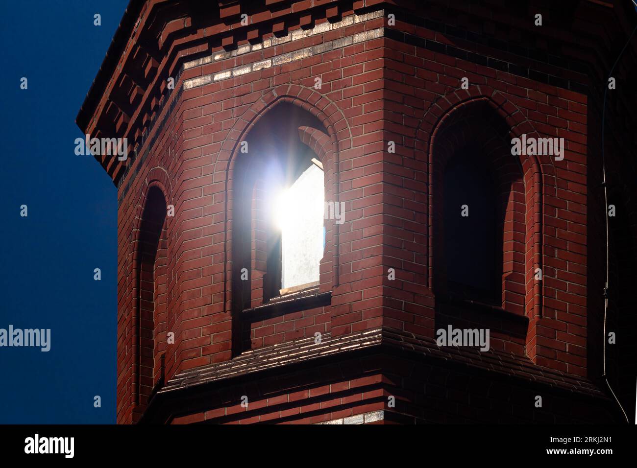 A tall, dark brick tower illuminated by a small window of sunlight ...