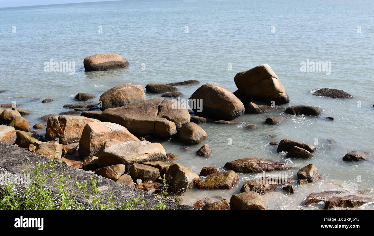 A scenic landscape featuring a beach shoreline with large rocky stones ...