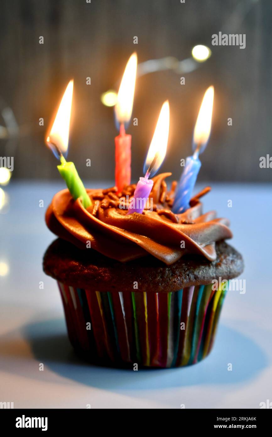 Chocolate cupcake with four colorful lit birthday candles Stock Photo ...
