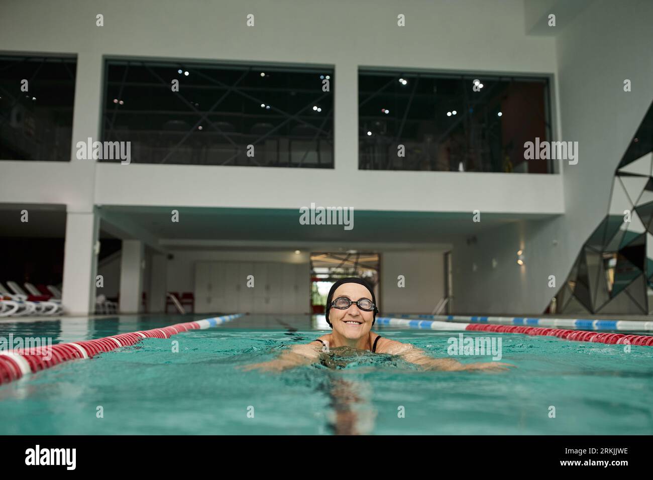 Cheerful Middle Aged Woman In Swim Cap And Goggles Swimming In Pool