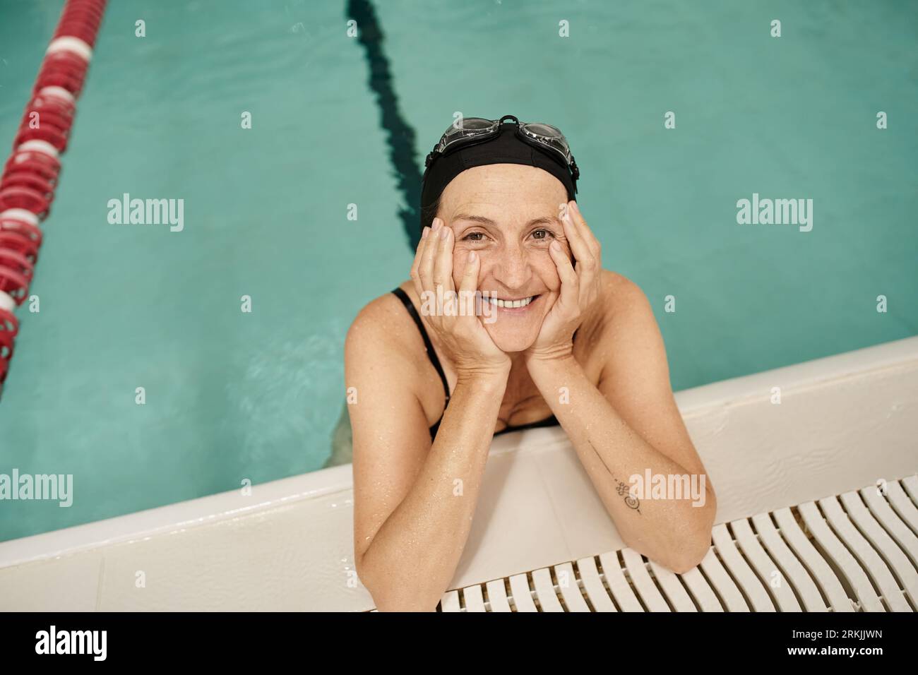 Top View Of Happy Middle Aged Woman In Swim Cap And Goggles Water In