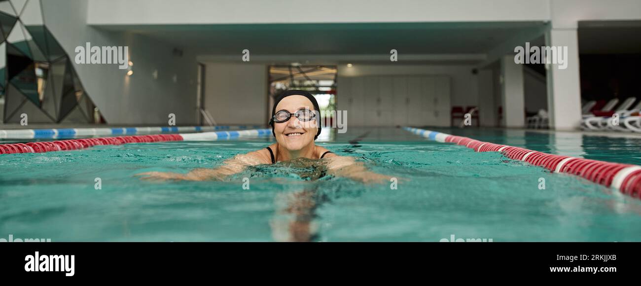 Cheerful Middle Aged Woman In Swim Cap And Goggles Swimming In Pool