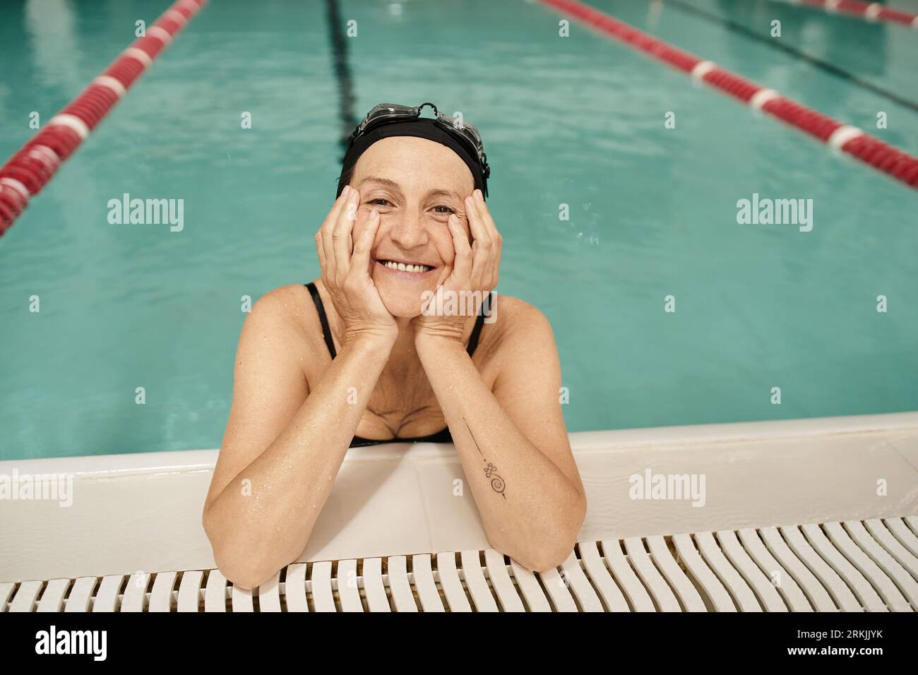 Joyous Middle Aged Woman In Swim Cap And Goggles Looking At Camera