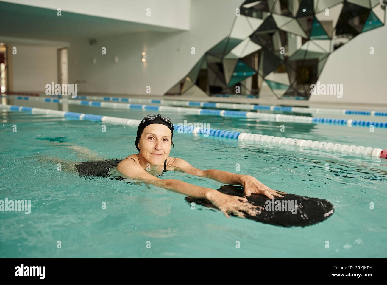 Middle Aged Woman Swimming With Floating Board In Pool Swim Cap And