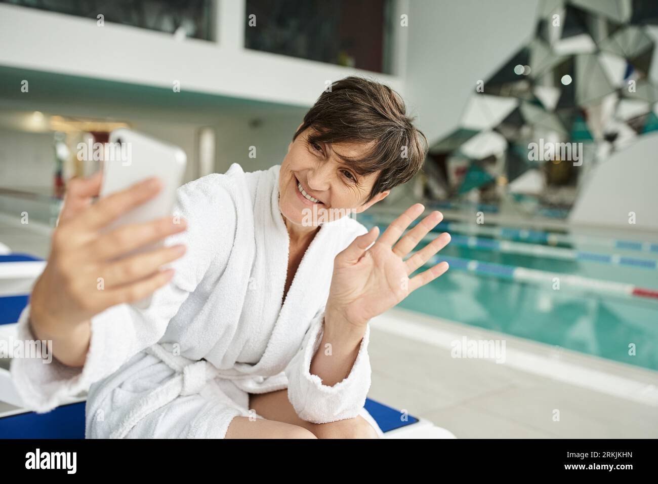 positive middle aged woman having video chat on smartphone, wave hand ...