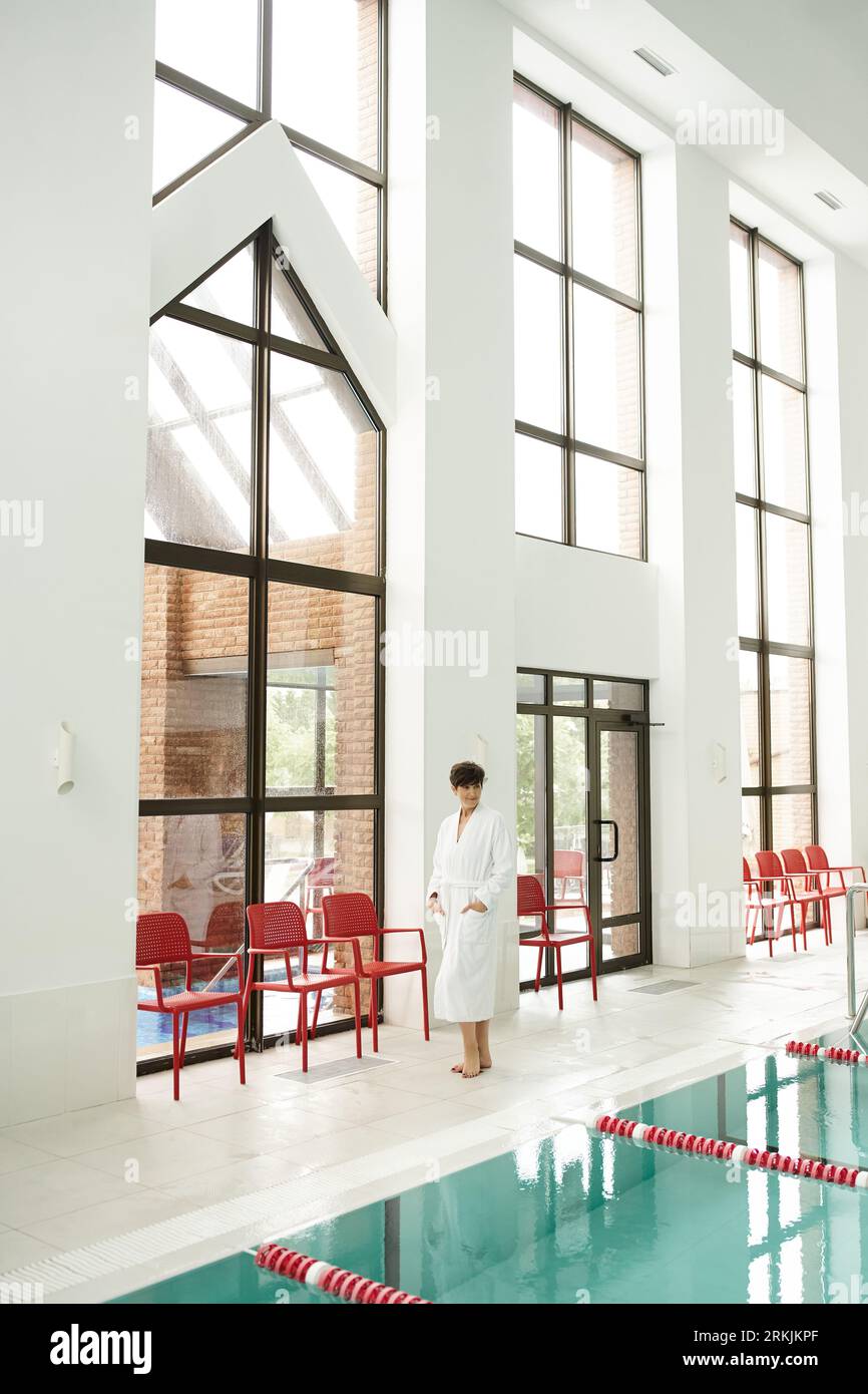modern spa center with swimming pool, mature woman in white robe, hands ...