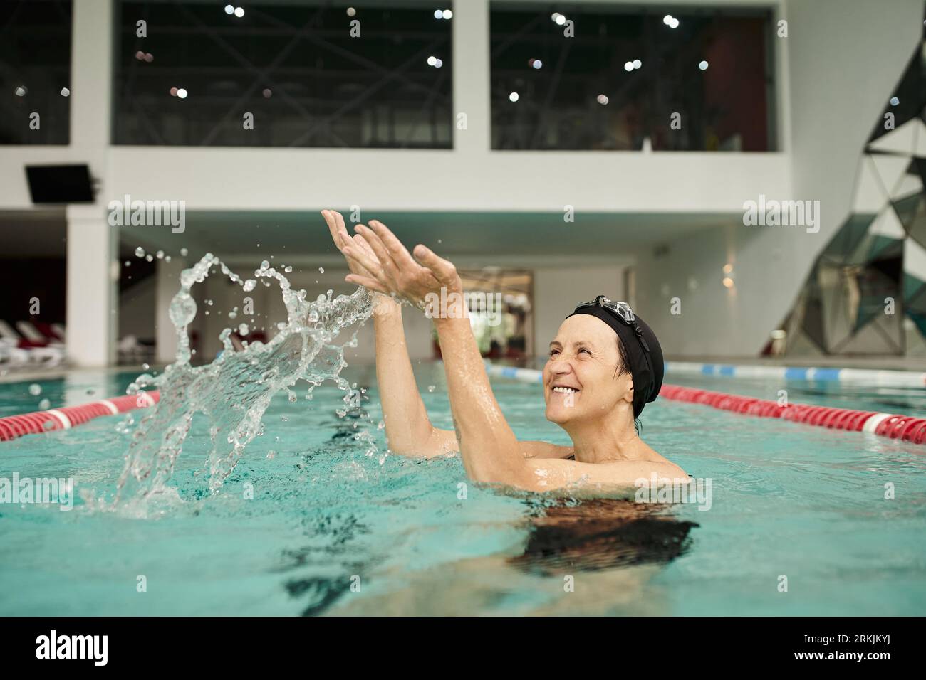 Water Splash Cheerful Middle Aged Woman In Swim Cap And Goggles Having