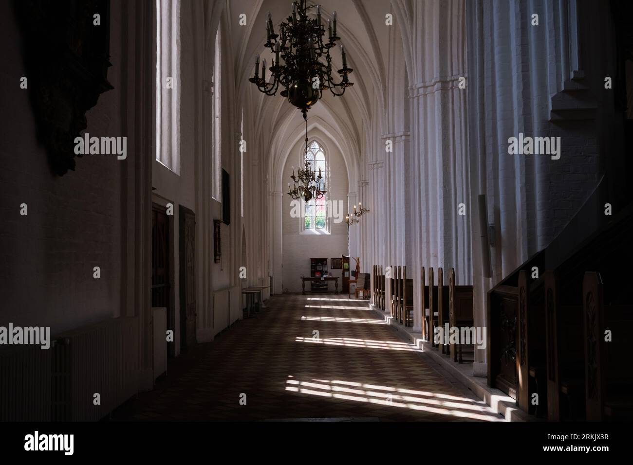 Interior of a simple cathedral, white corridors and dark wooden pews ...
