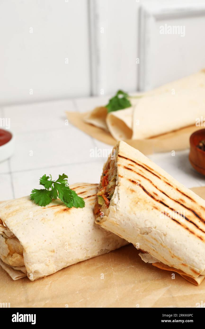 Baking paper with tasty shawarma with parsley on white tile table Stock ...