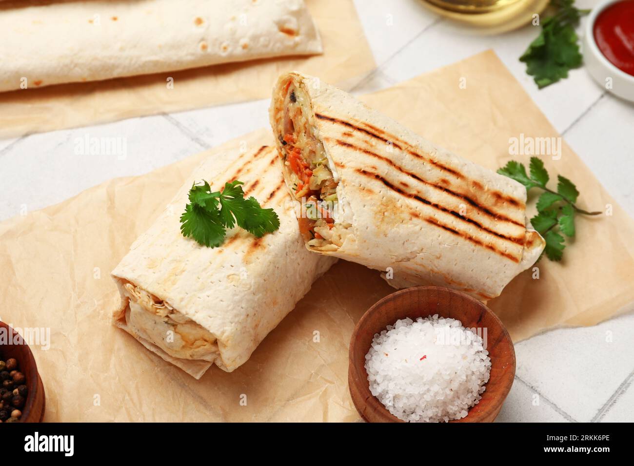Baking paper with tasty shawarma with parsley on white tile table Stock ...