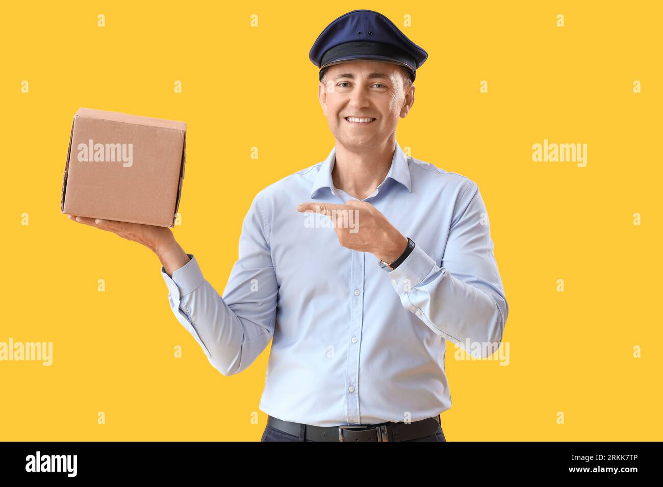 Mature postman pointing at parcel on yellow background Stock Photo - Alamy