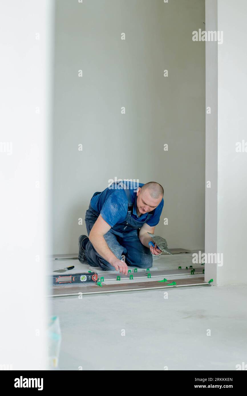 Tiler placing ceramic wall tile in position over adhesive with lash ...