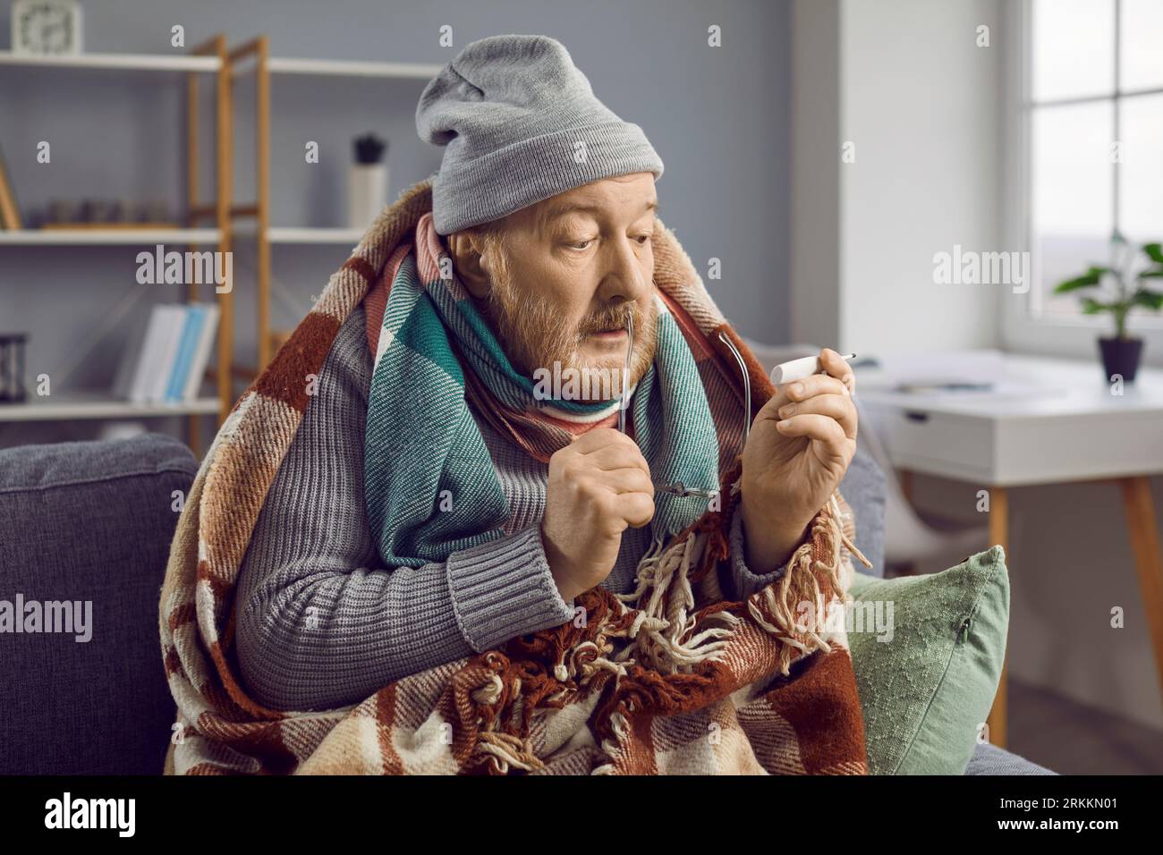 Sick senior man with high temperature looking at thermometer with ...