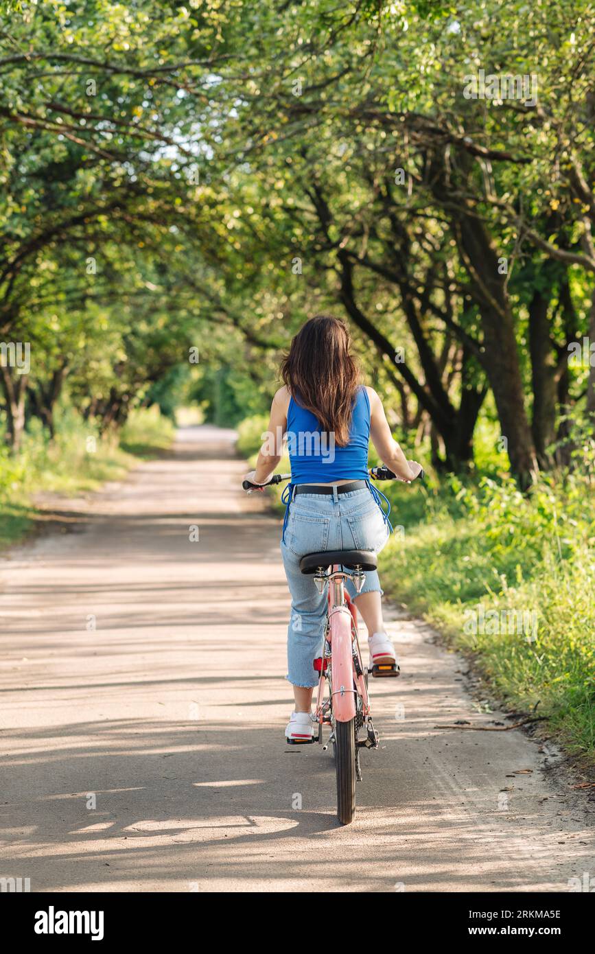 Rear back view of a young woman riding a bike in a city park at ...