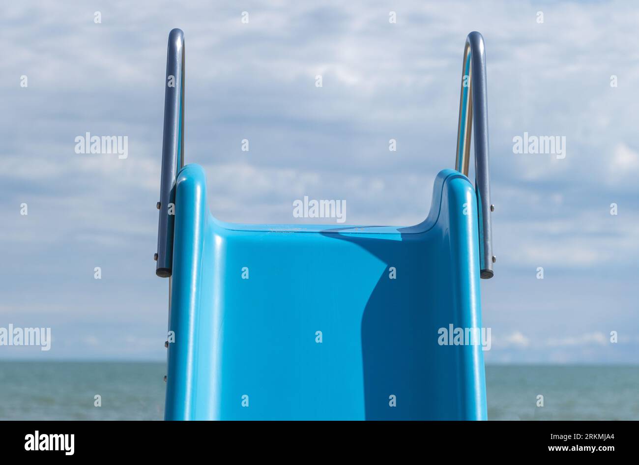 Blue plastic slide on the beach, blue sky and white clouds background ...
