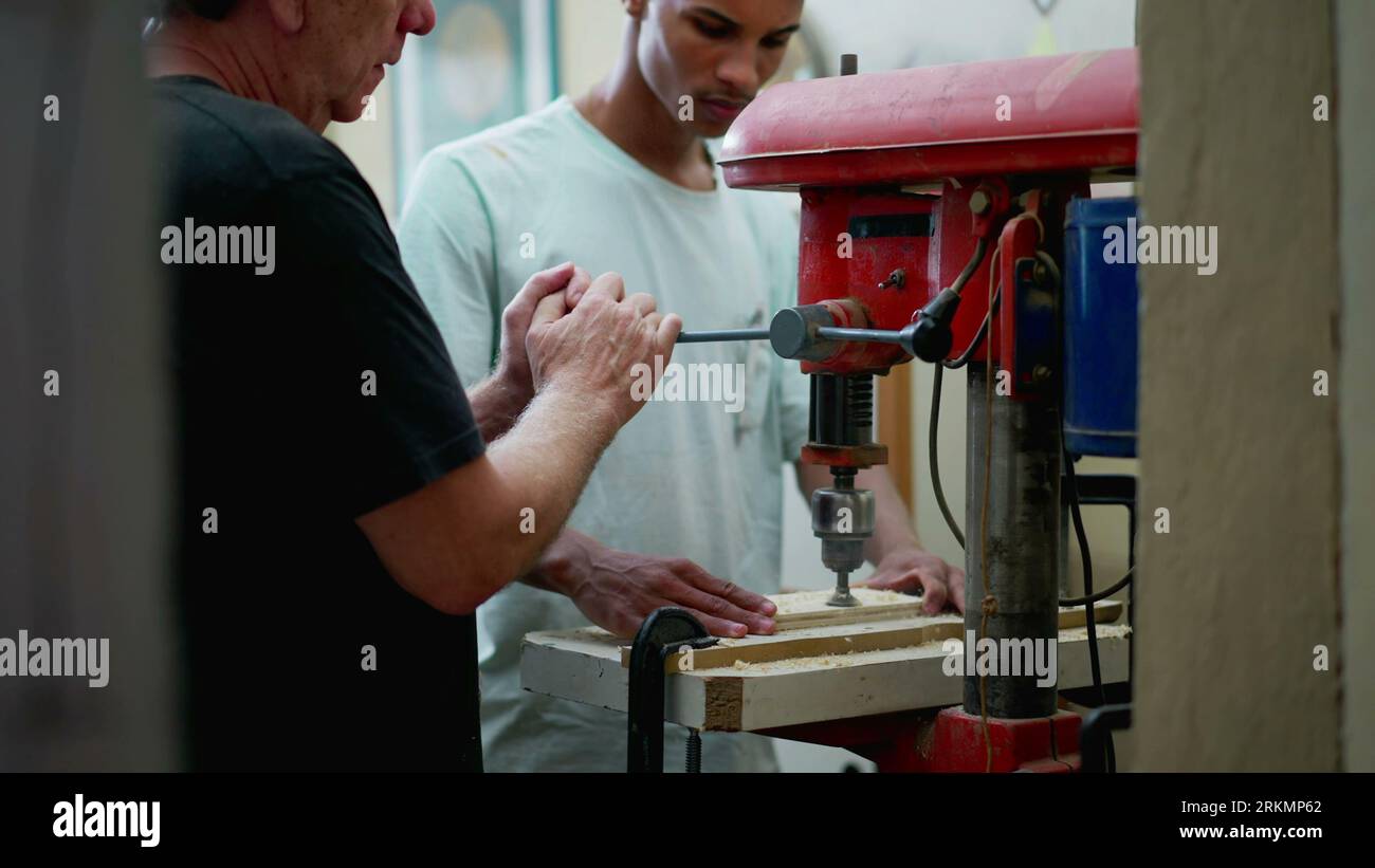 Senior staff guiding carpentry apprentice to use machine at workshop ...