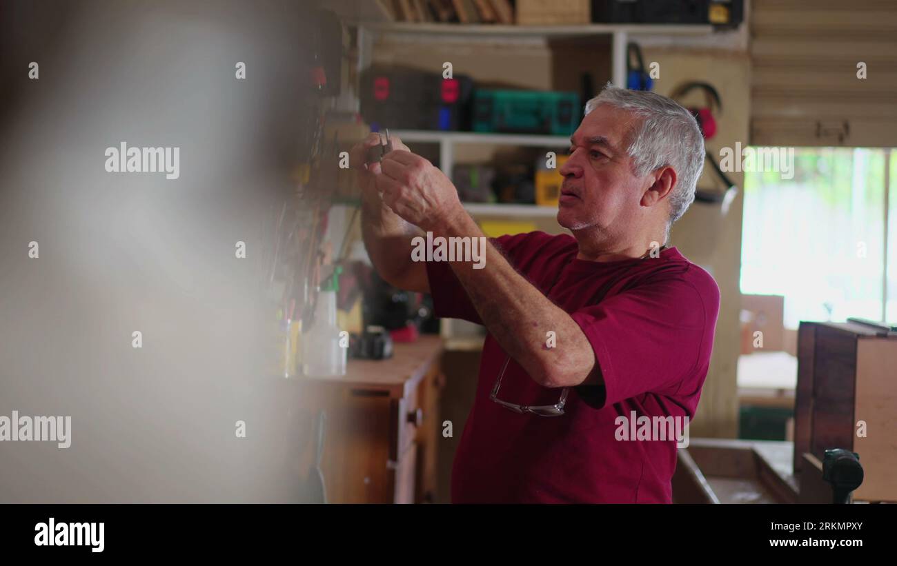 Older man working at workshop, grabbing tools from wall and engaged ...