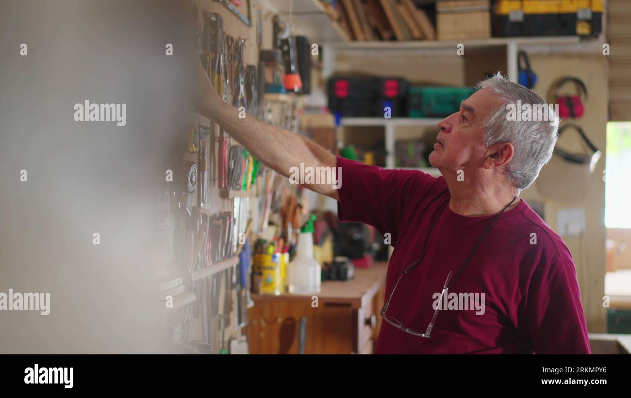 Older man working at workshop, grabbing tools from wall and engaged ...