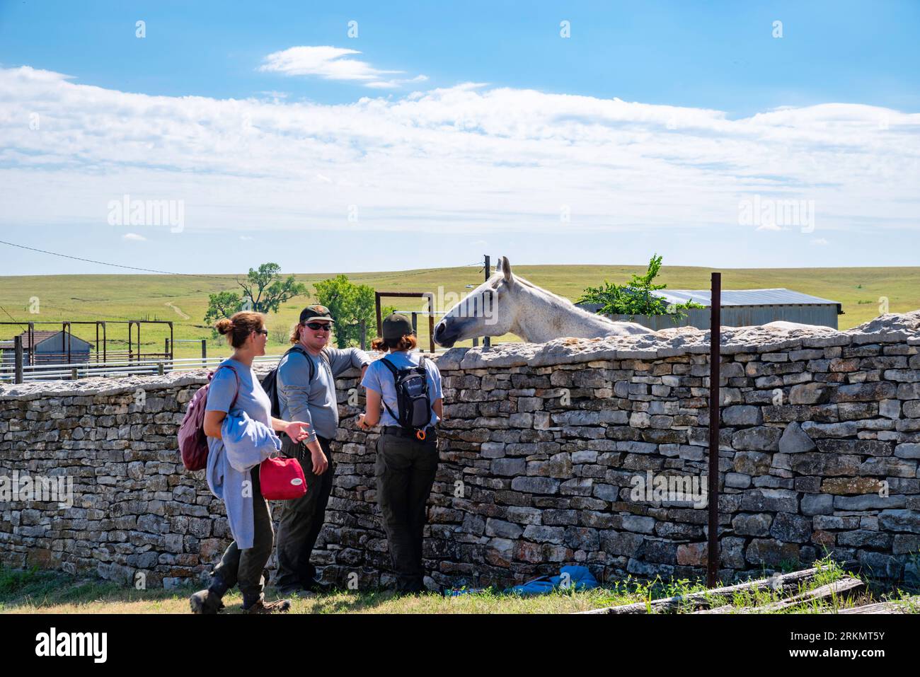 Three park employees feed a horse over a stone fence at Tallgrass ...