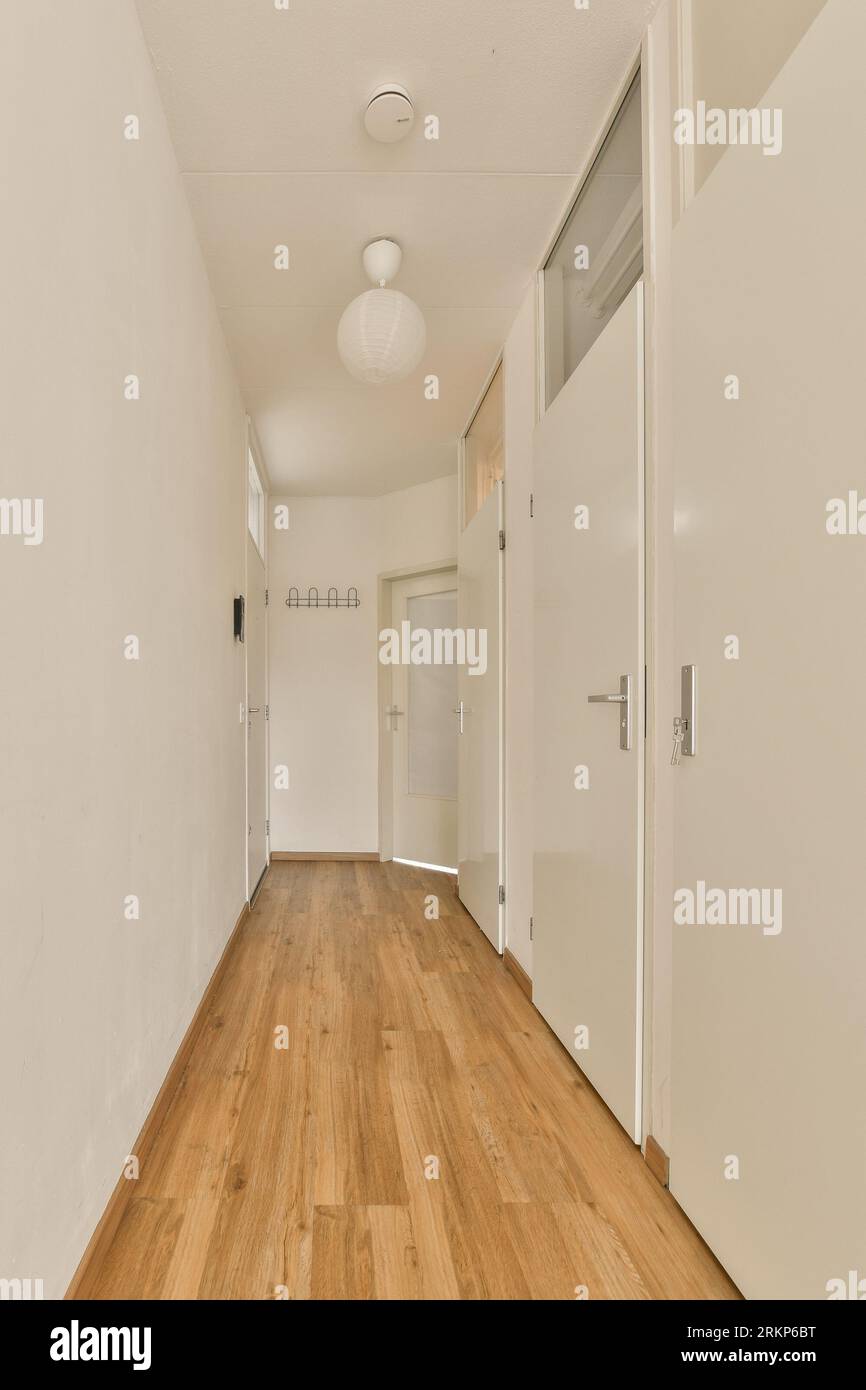 a long hallway with white walls and wood flooring on the right side ...