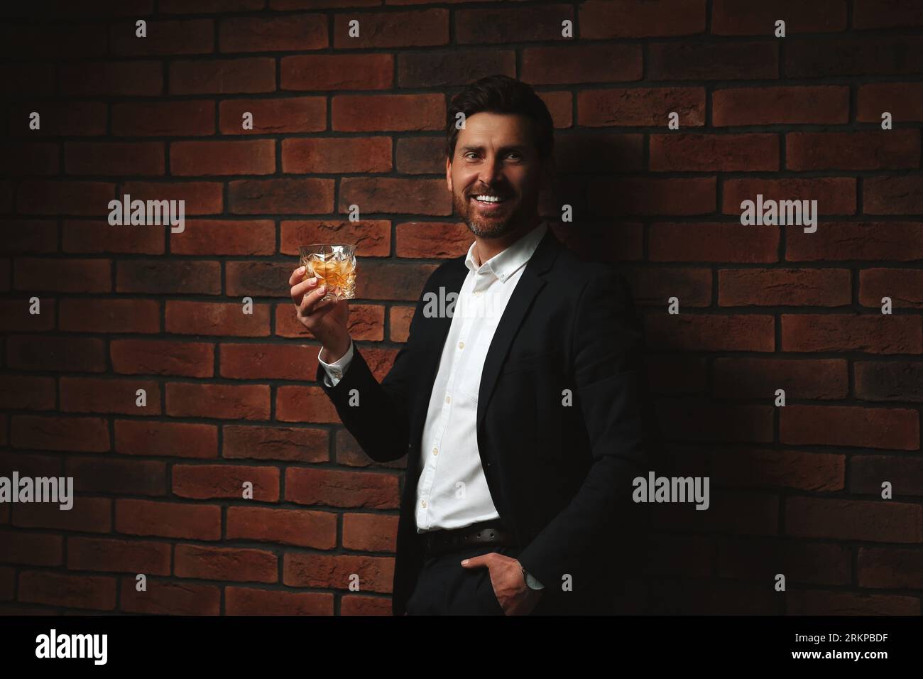 Man in formal suit holding glass of whiskey near red brick wall Stock ...